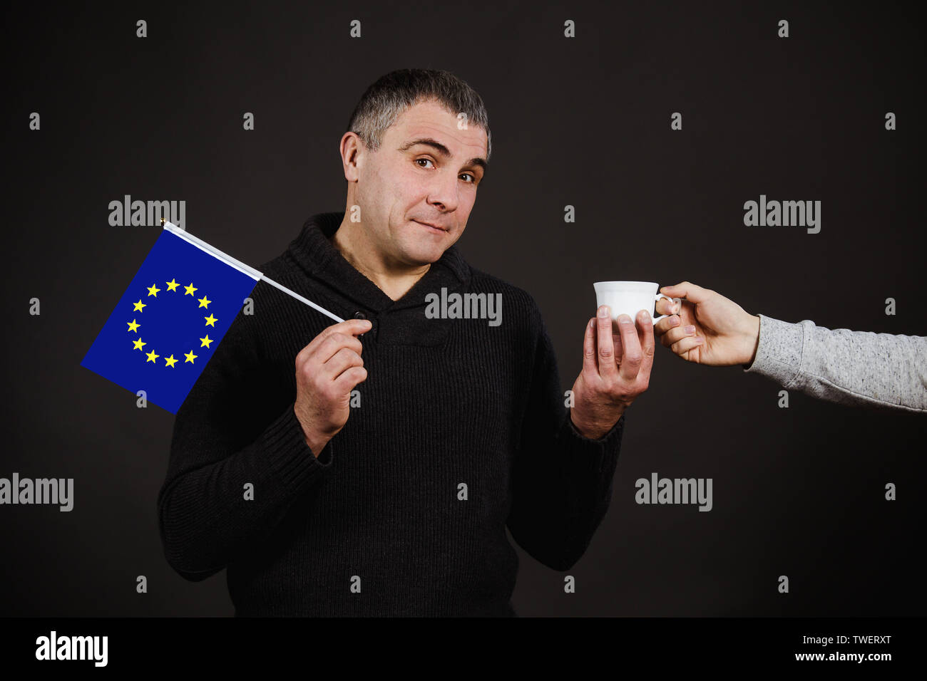 Man holding EU flag. Man in a dark sweater on a black background holds ...