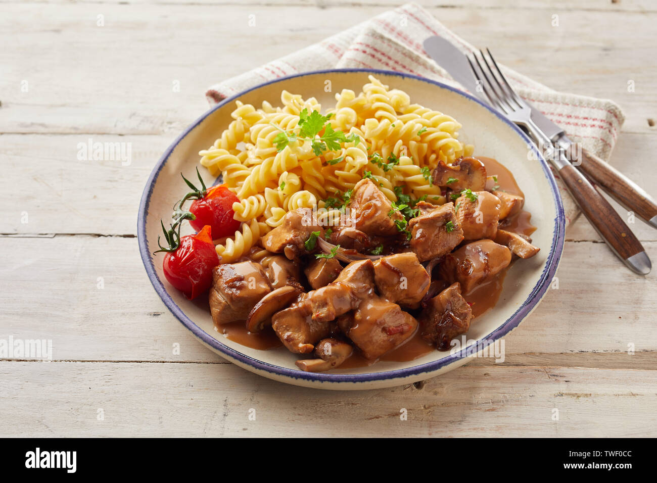 Hot plate of pasta with herbs and sauce on diced meat next to metal ...