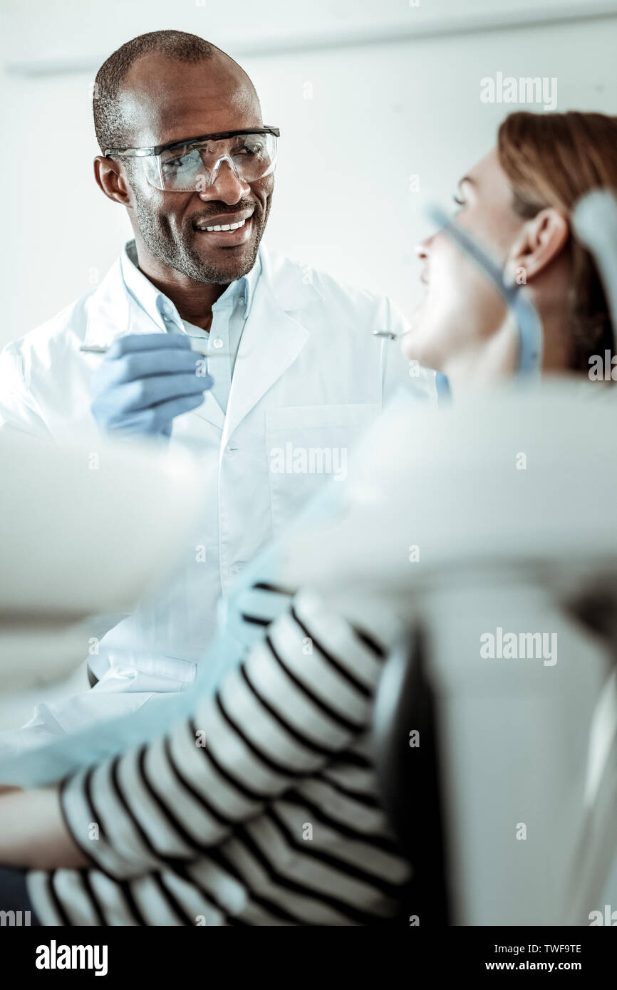 Distracting her attention. Professional dark-skinned dentist asking his ...