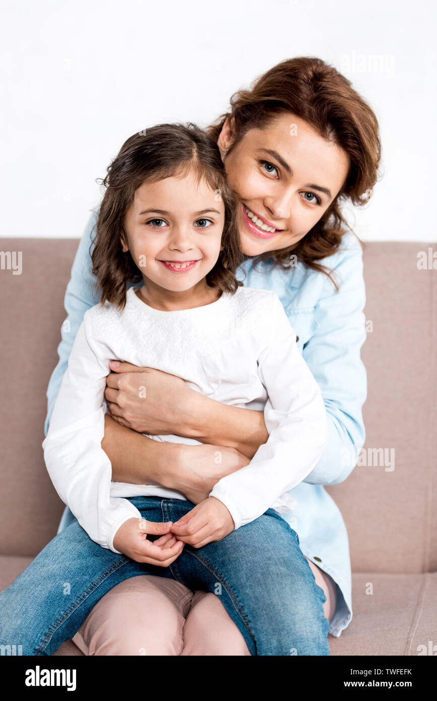 Laughing mother sitting on sofa and holding daughter on knees isolated ...