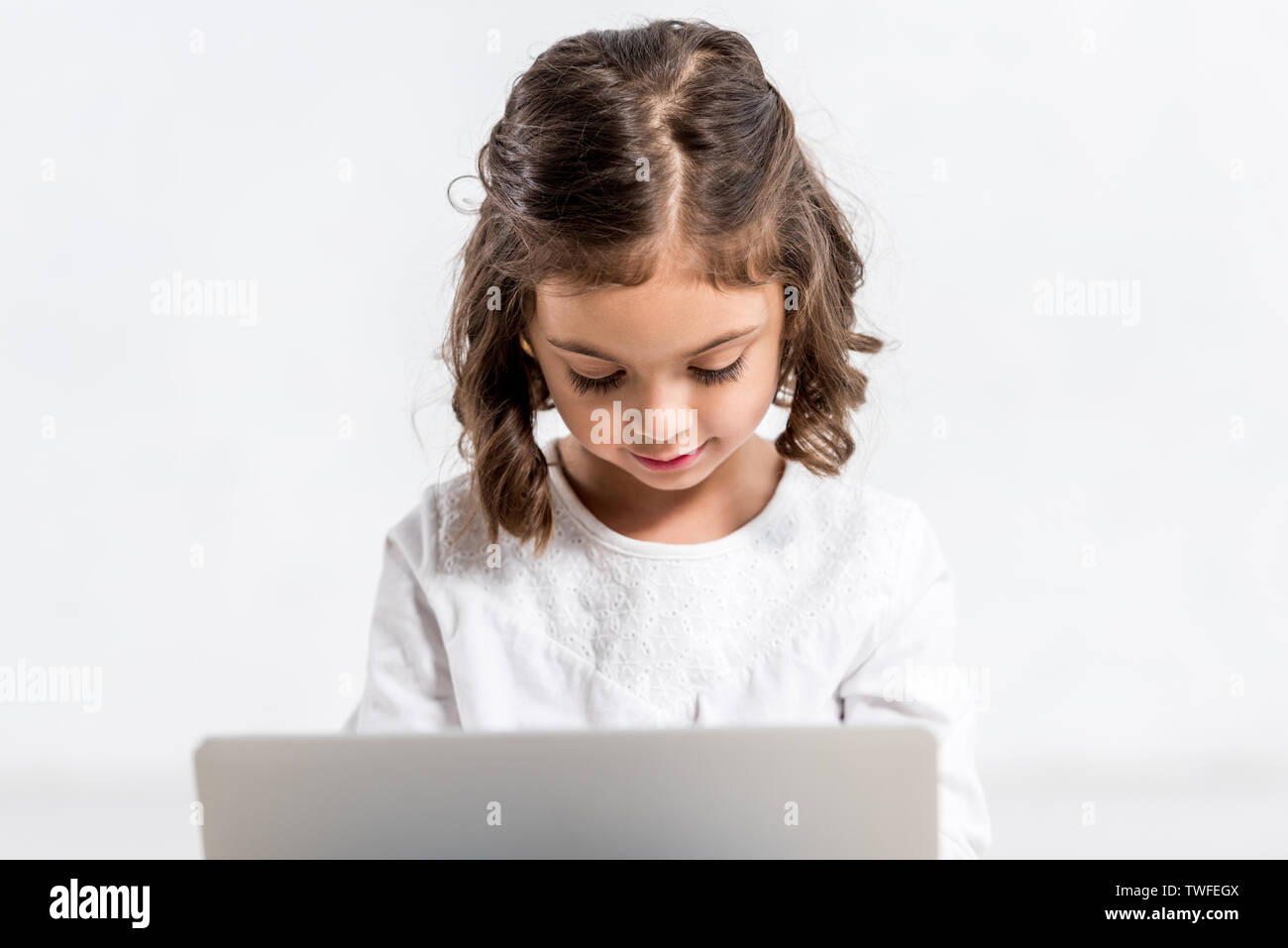 Concentrated kid looking down while using laptop on white Stock Photo ...