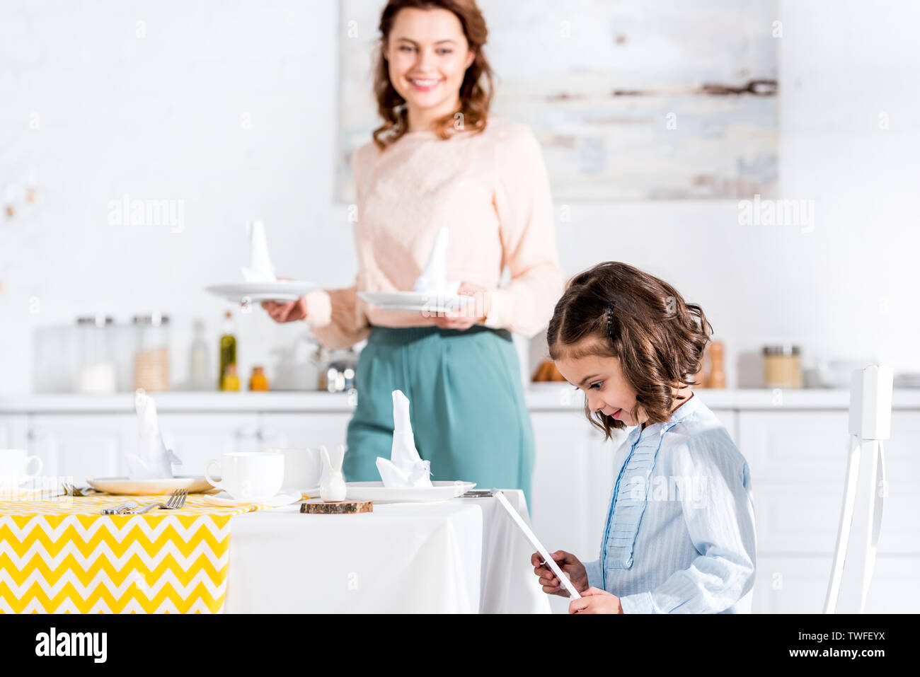 Child using digital tablet while mother serving table in kitchen Stock ...