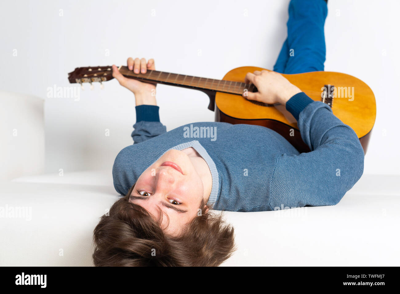 Happy young man lying back on sofa with guitar. Smiling guitarist ...