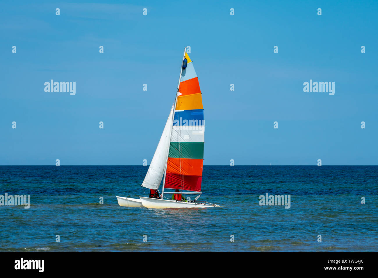 catamaran sailing boat with a very colourful sail with 7 different ...