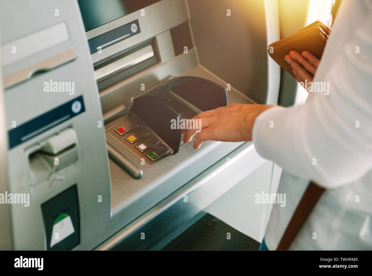 Woman using ATM holding wallet an pressing the PIN security number on ...