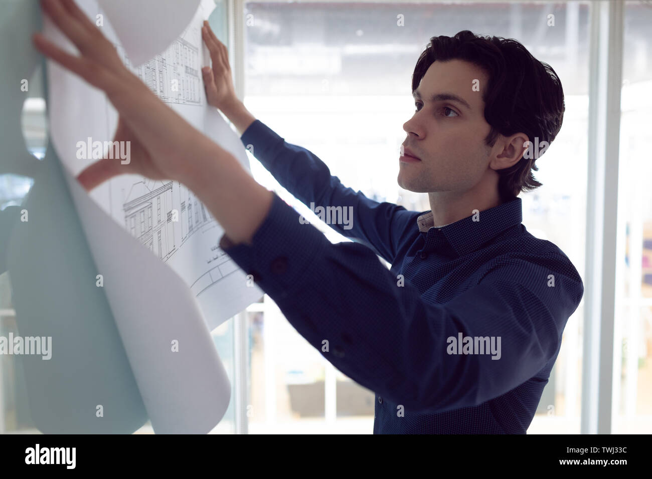 Male architect looking at blueprint in office Stock Photo - Alamy