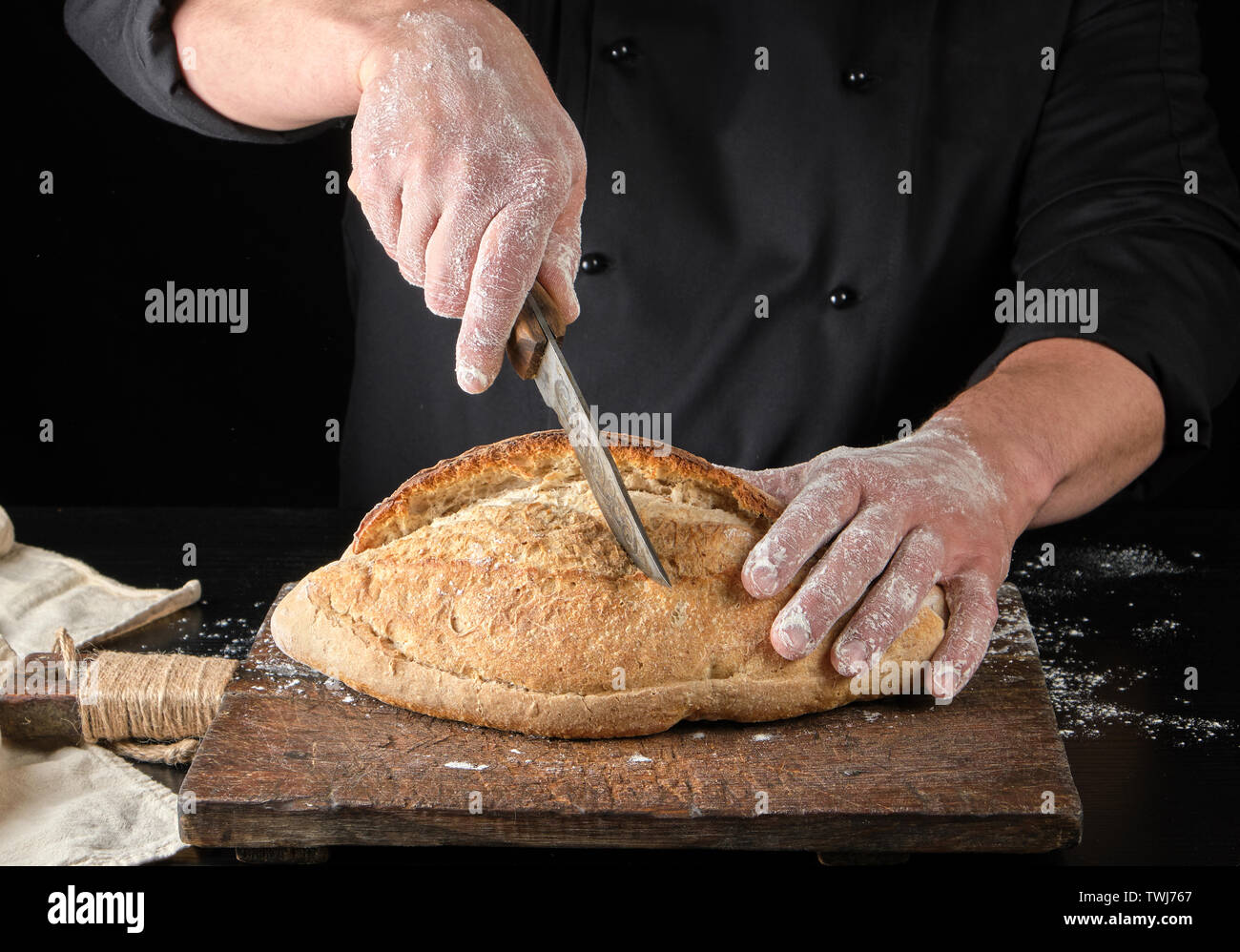 chef in black uniform cuts baked white wheat flour oval bread on brown ...