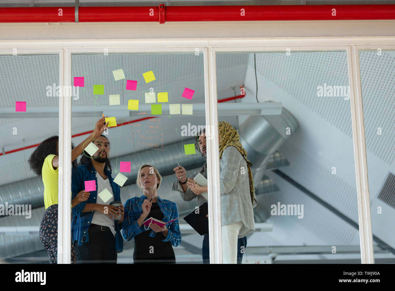Business people discussing over sticky notes on glass wall in a modern ...