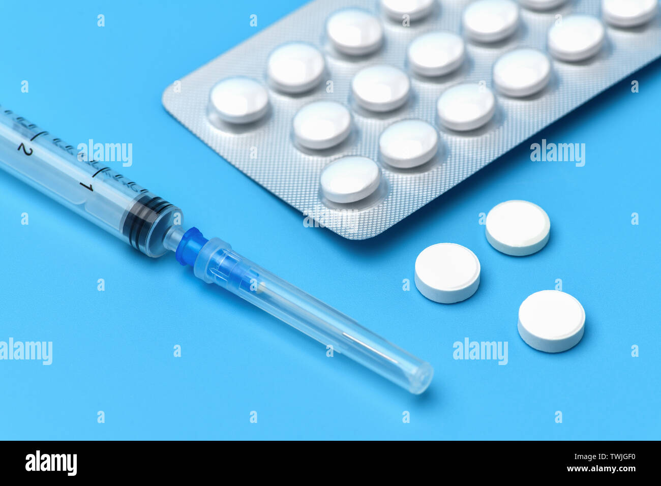 Many tablets are on a blue background, at the bottom is a syringe with ...