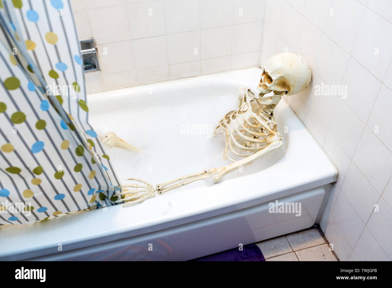 Bony skeleton taking a bubble bath in a grungy off-white dirty tub ...
