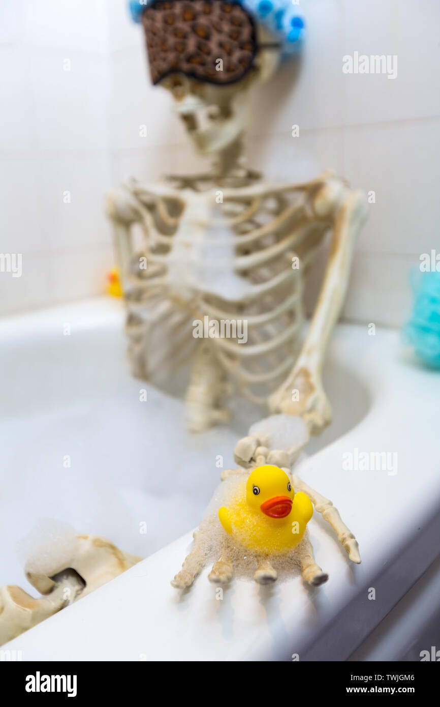 Bony skeleton taking a bubble bath in a grungy off-white dirty tub ...