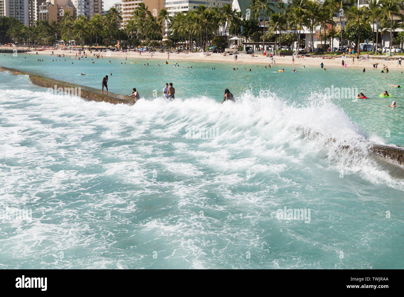 The incoming waves hit the seawall while tourists and locals walk on it ...