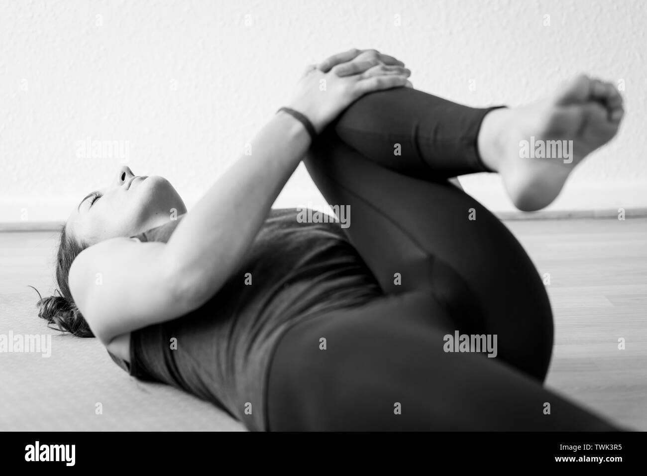 A woman in her early 30's doing yoga on the floor, performing the ...