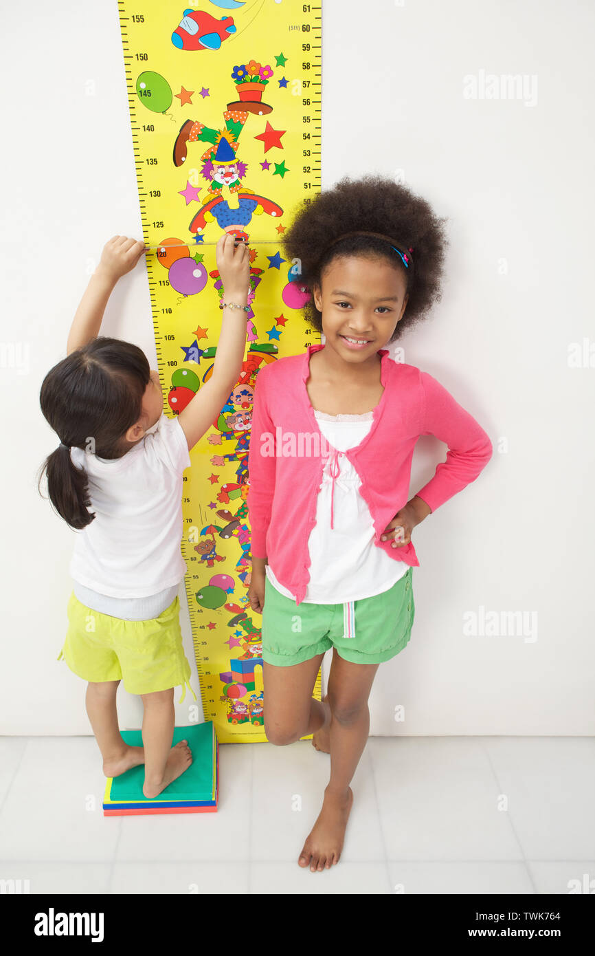 Little girl measuring height of her sister Stock Photo - Alamy