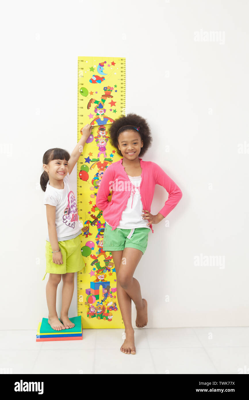 Little girl measuring height of her friend Stock Photo - Alamy