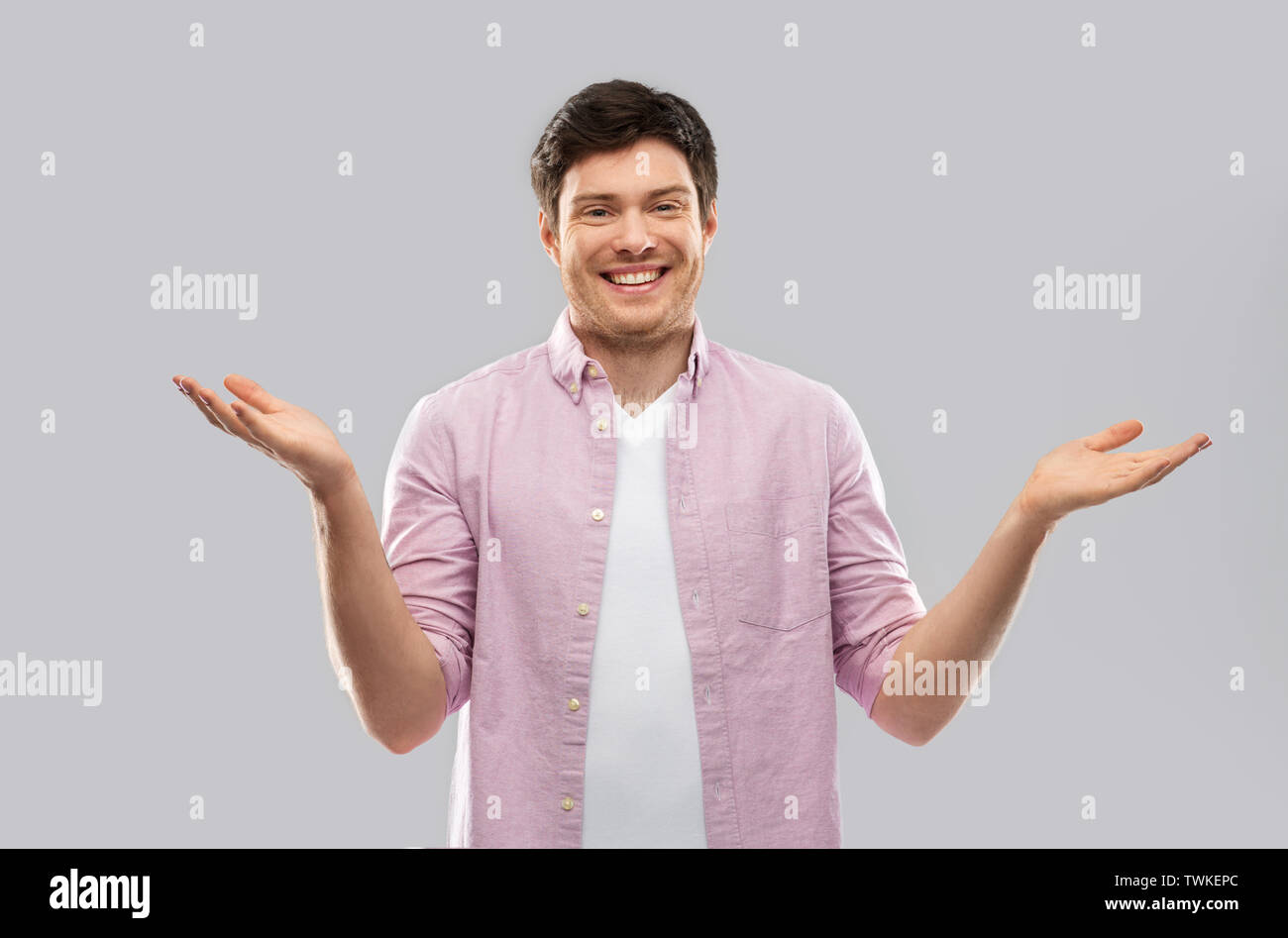 happy young man shrugging over grey background Stock Photo - Alamy
