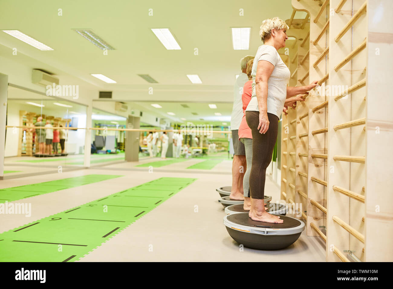 Senior group doing balance training in physiotherapy on the wall bars ...