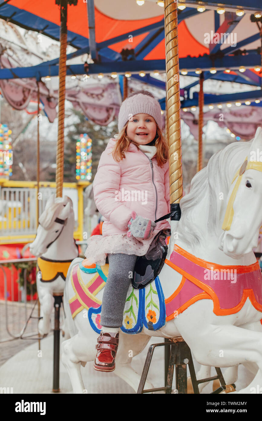 Adorable smiling Caucasian child girl riding on merry go round carousel ...