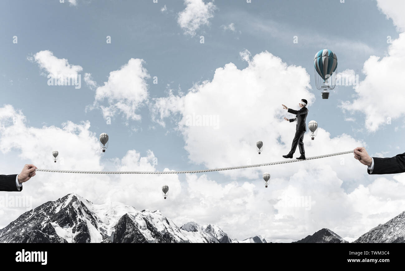 Businessman walking blindfolded on rope above high mountains as symbol ...