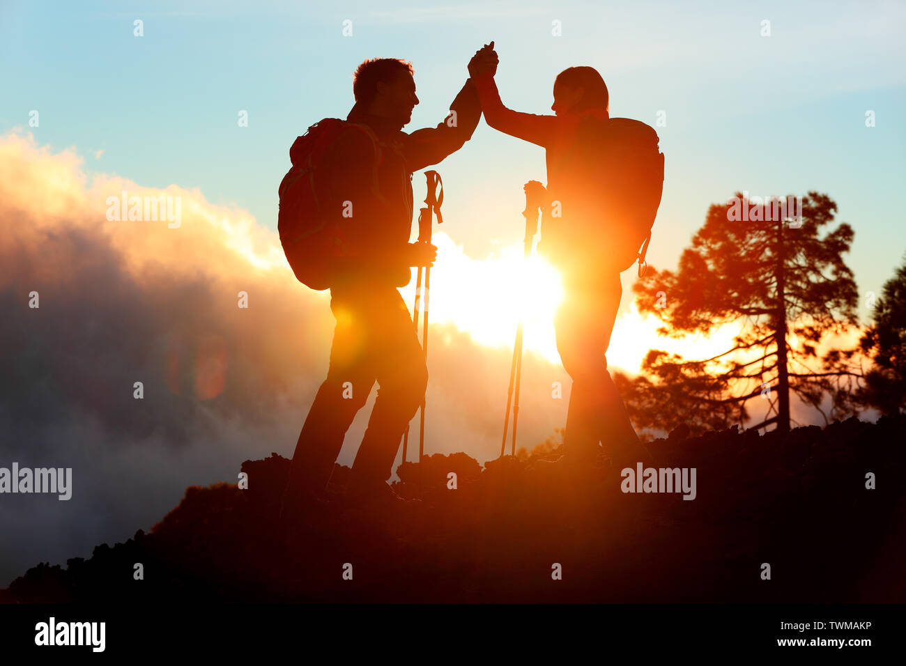 Hiking people reaching summit top giving high five at mountain top at sunset. Happy hiker couple ...