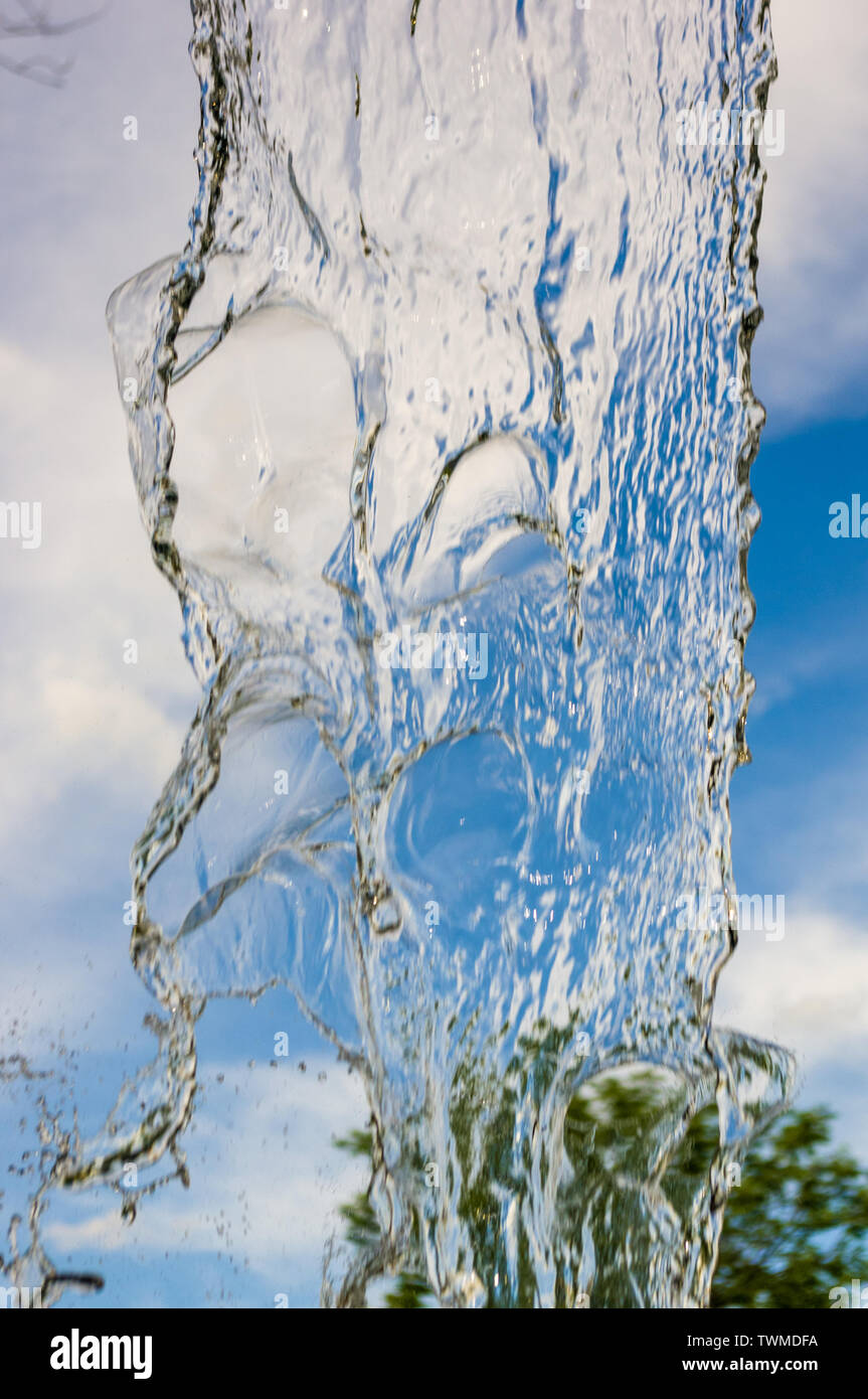 transparent falling water vertical flows against a blue sky and green ...