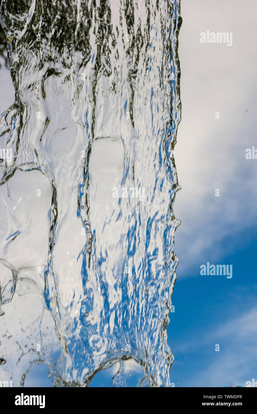 transparent falling water vertical flows against a blue sky and green ...