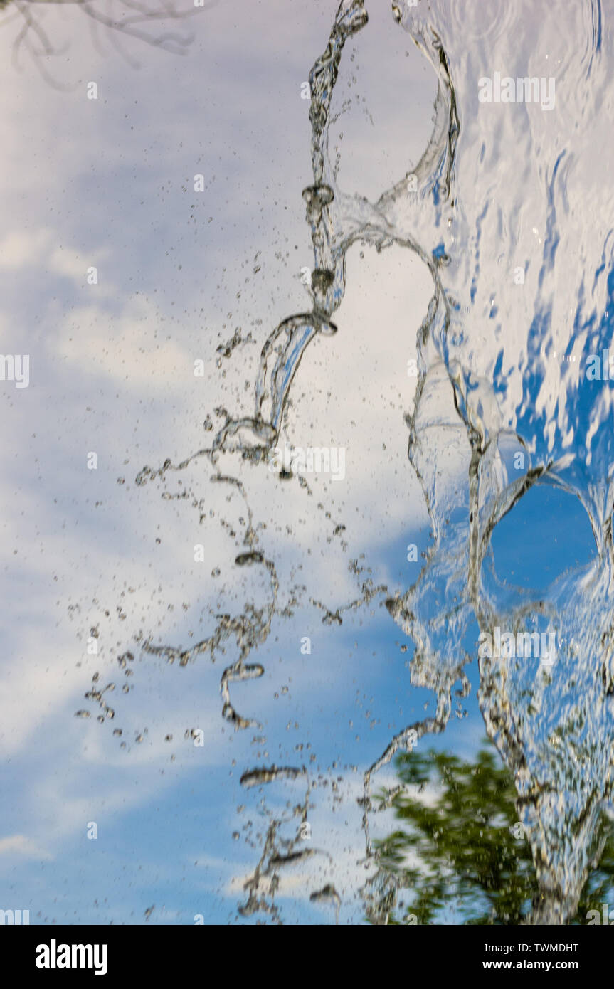transparent falling water vertical flows against a blue sky and green ...
