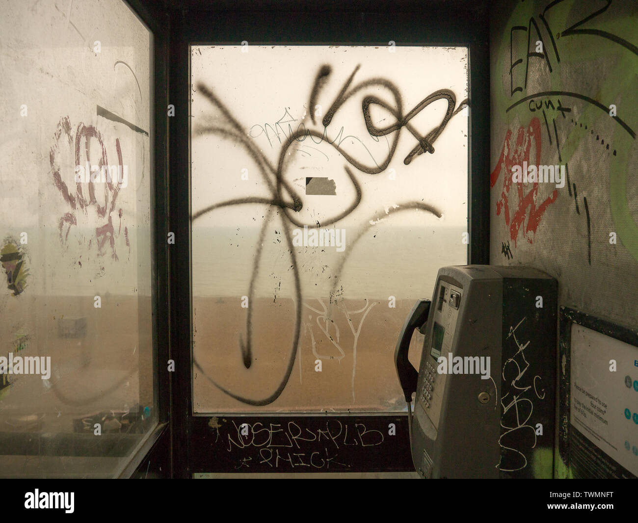 Colour image of a graffiti covered phone booth, with the sea and a ...