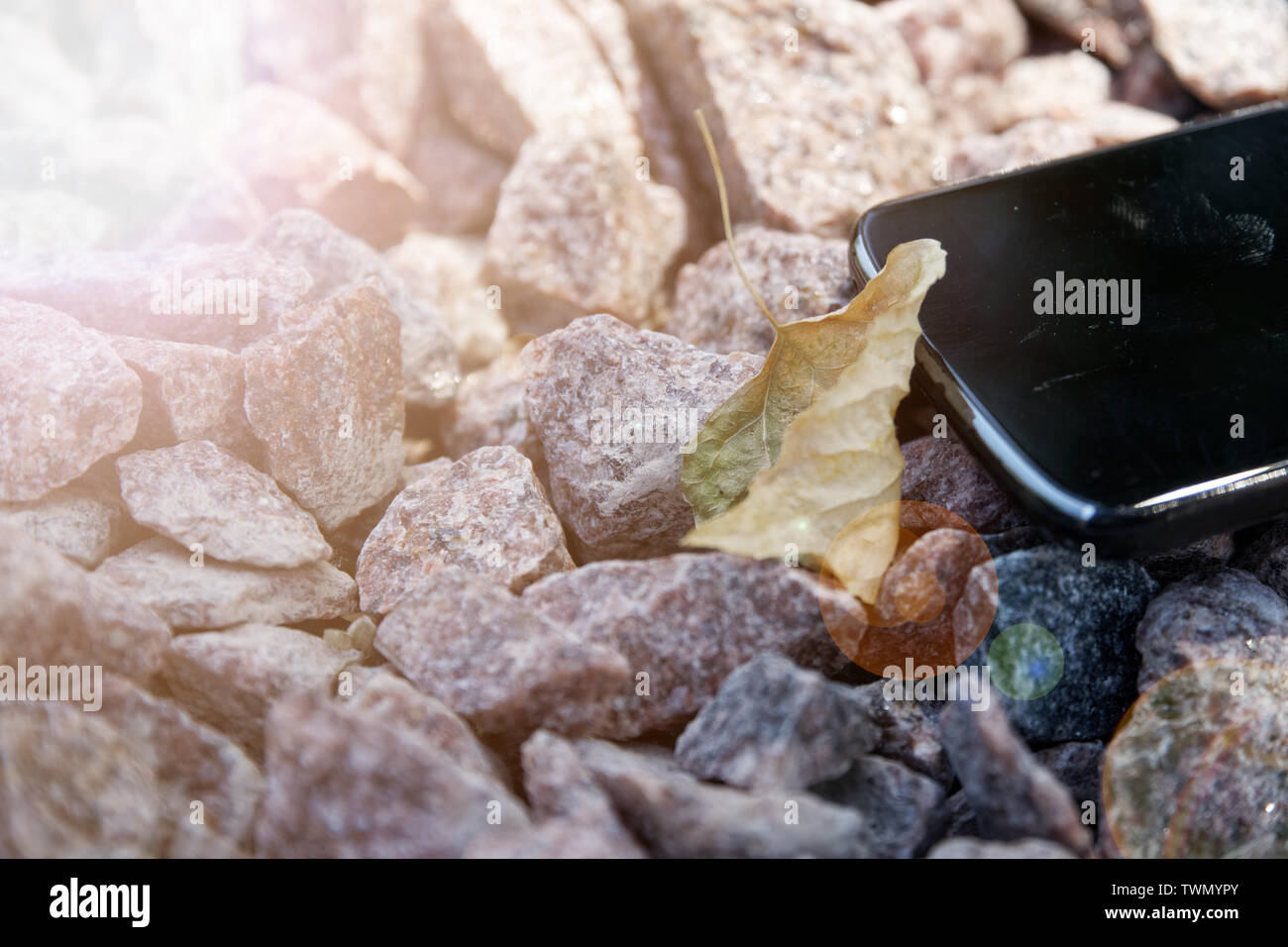Broken cellphone abandoned and lost among the gravel, with sun beam ...