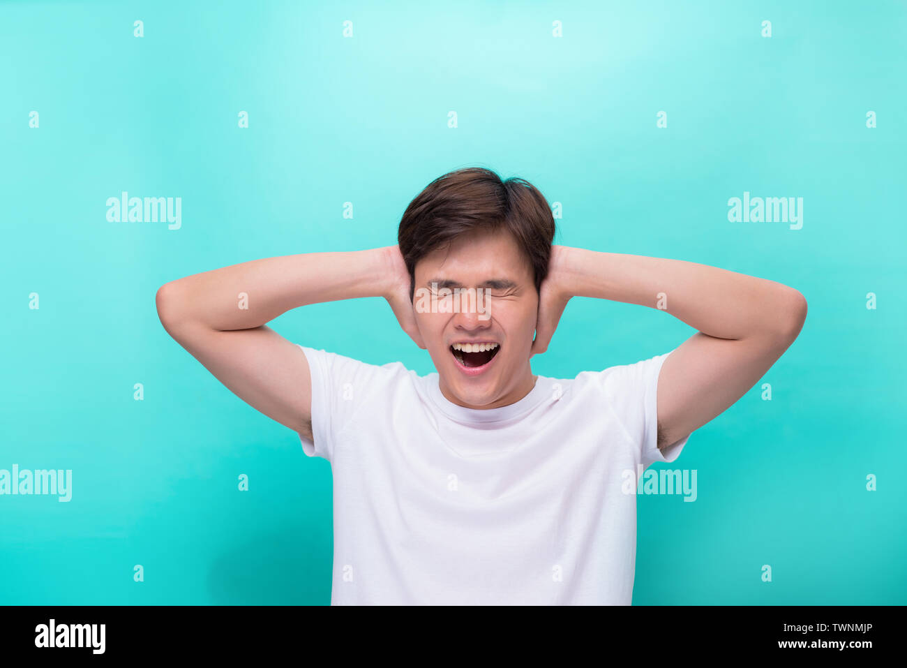 Too loud. Frustrated young man covering ears with hands and looking at ...