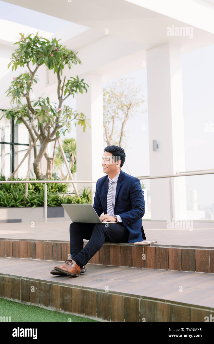 Happy young businessman using laptop outside office building Stock ...
