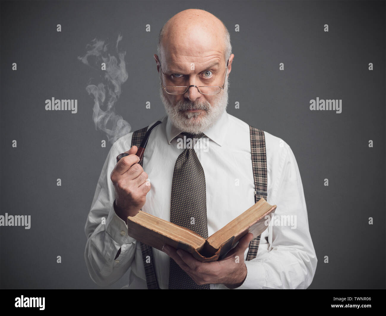 Confident senior professor smoking a pipe and reading an old book ...