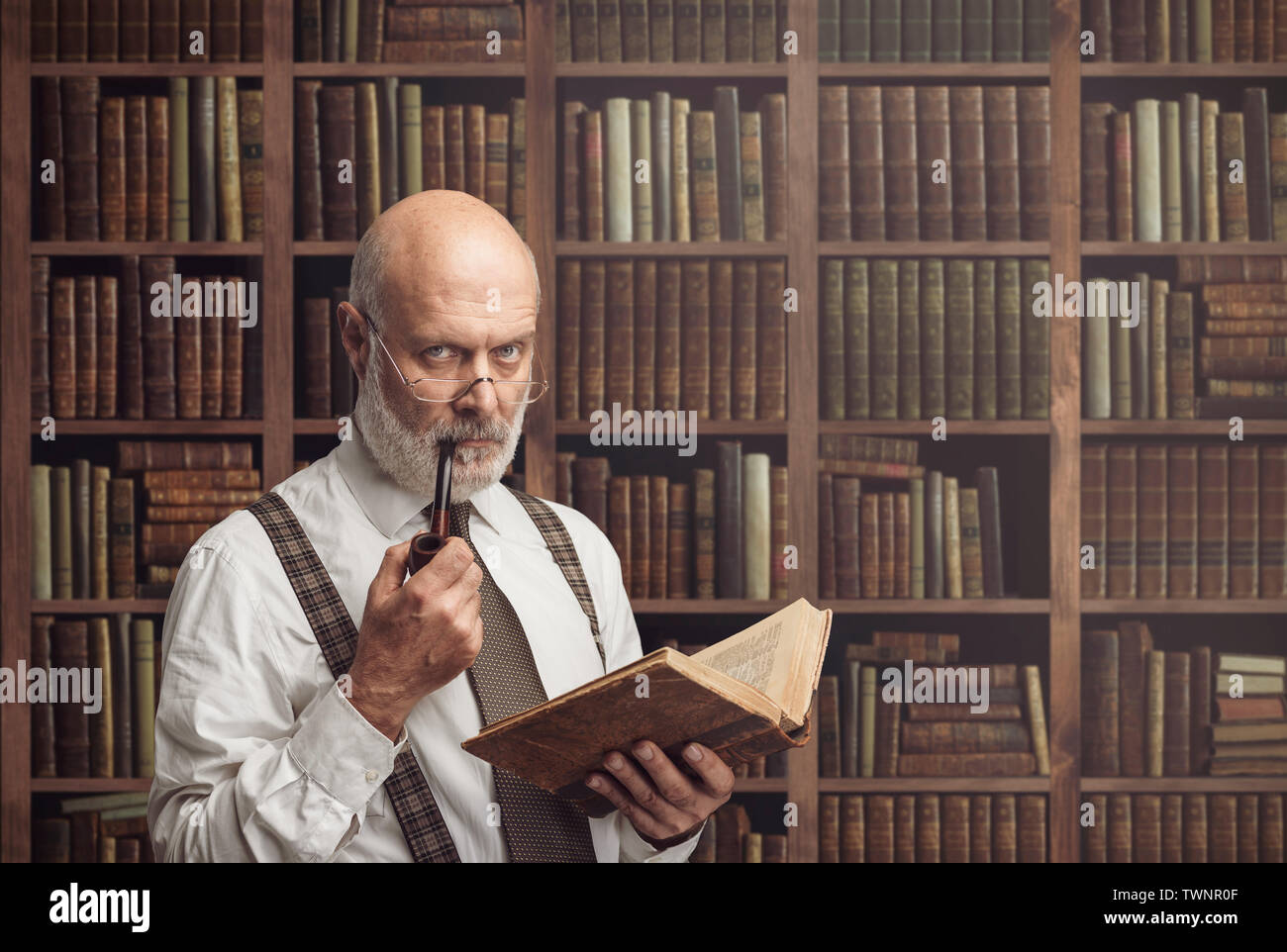 Senior academic professor reading an old book in the library, knowledge ...