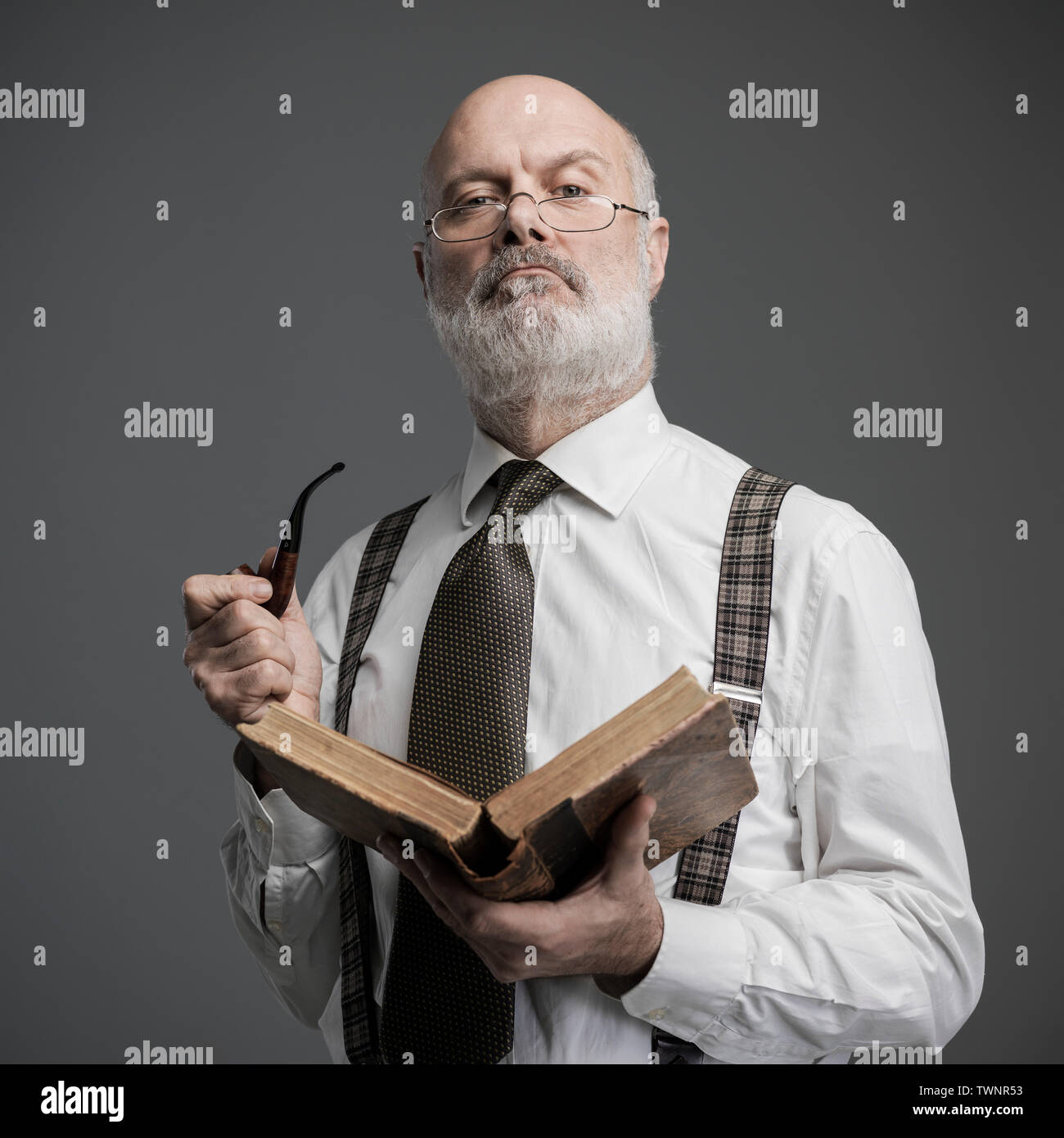 Confident senior professor smoking a pipe and reading an old book ...