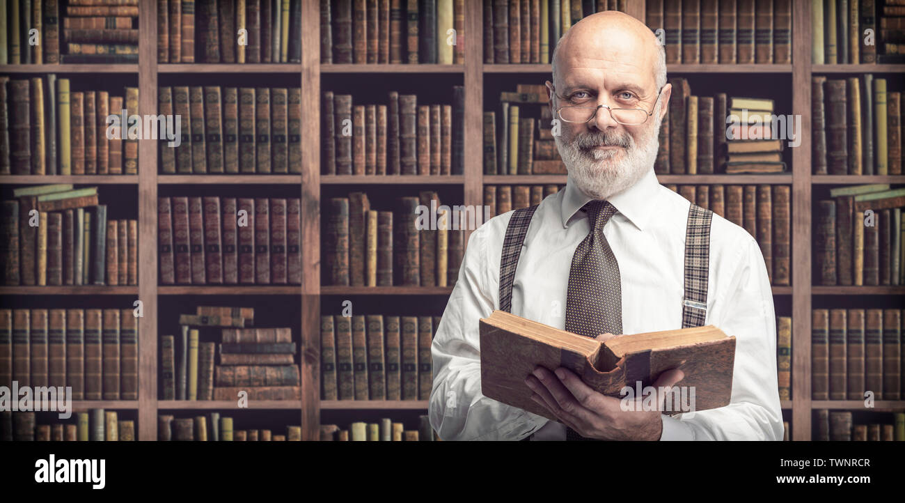 Senior academic professor reading an old book in the library, knowledge ...