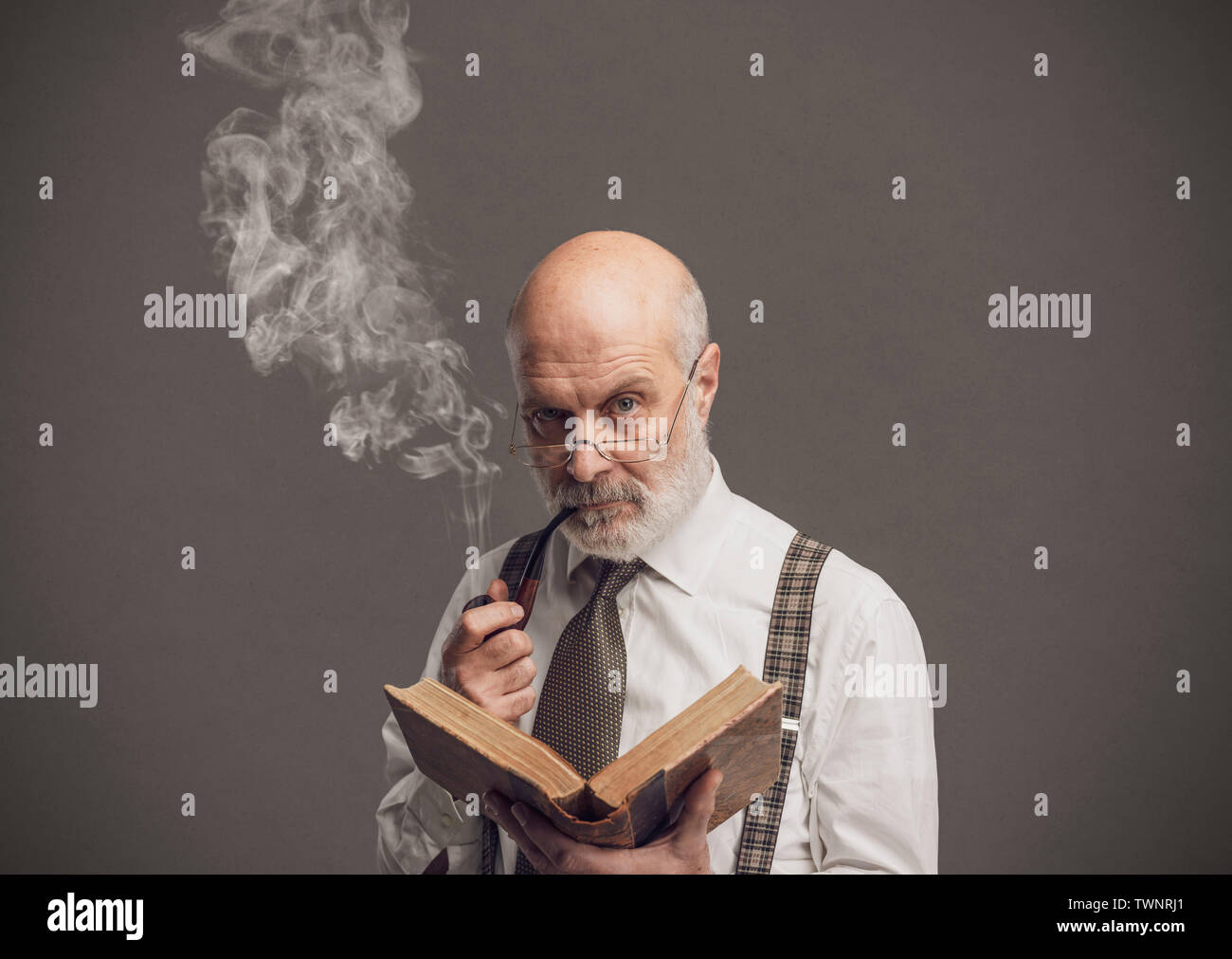 Confident senior professor smoking a pipe and reading an old book ...