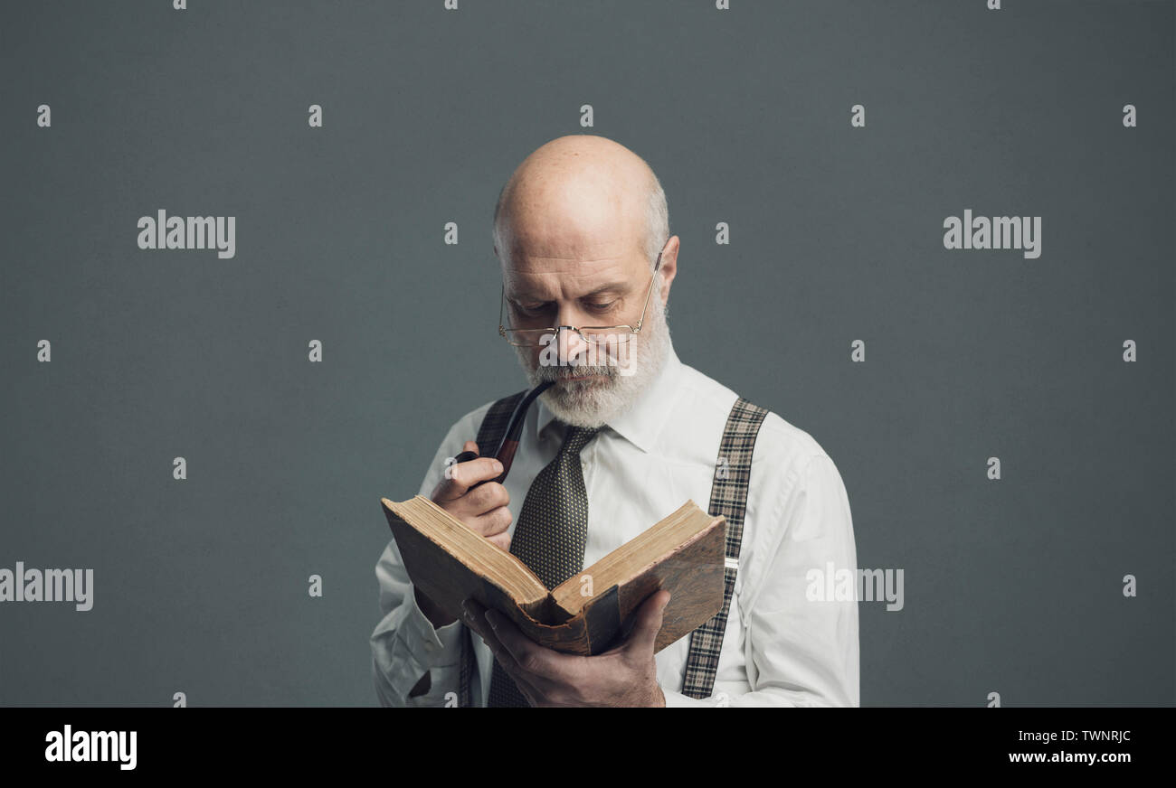 Confident senior professor smoking a pipe and reading an old book ...