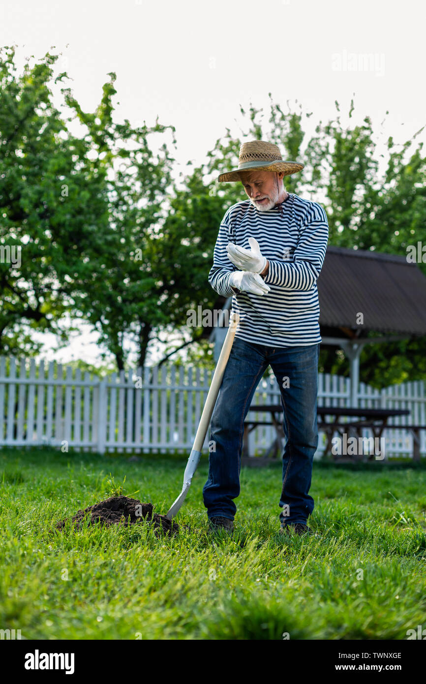 Working with shovel. Grey-haired man wearing gloves working with shovel ...