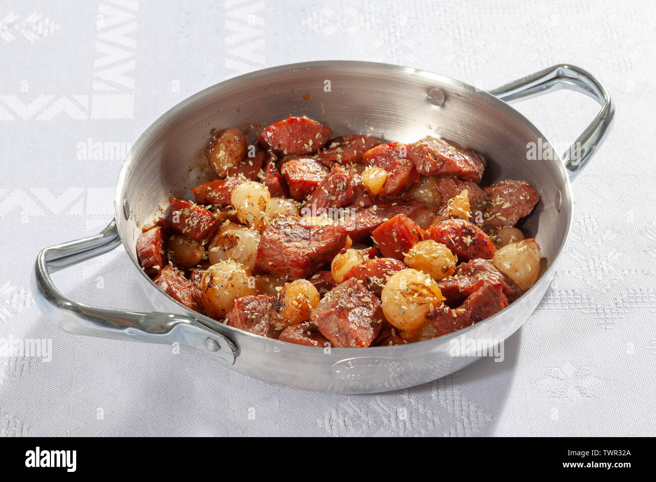 pieces of beef meat cooked with small onions in sliver colored fry pan ...