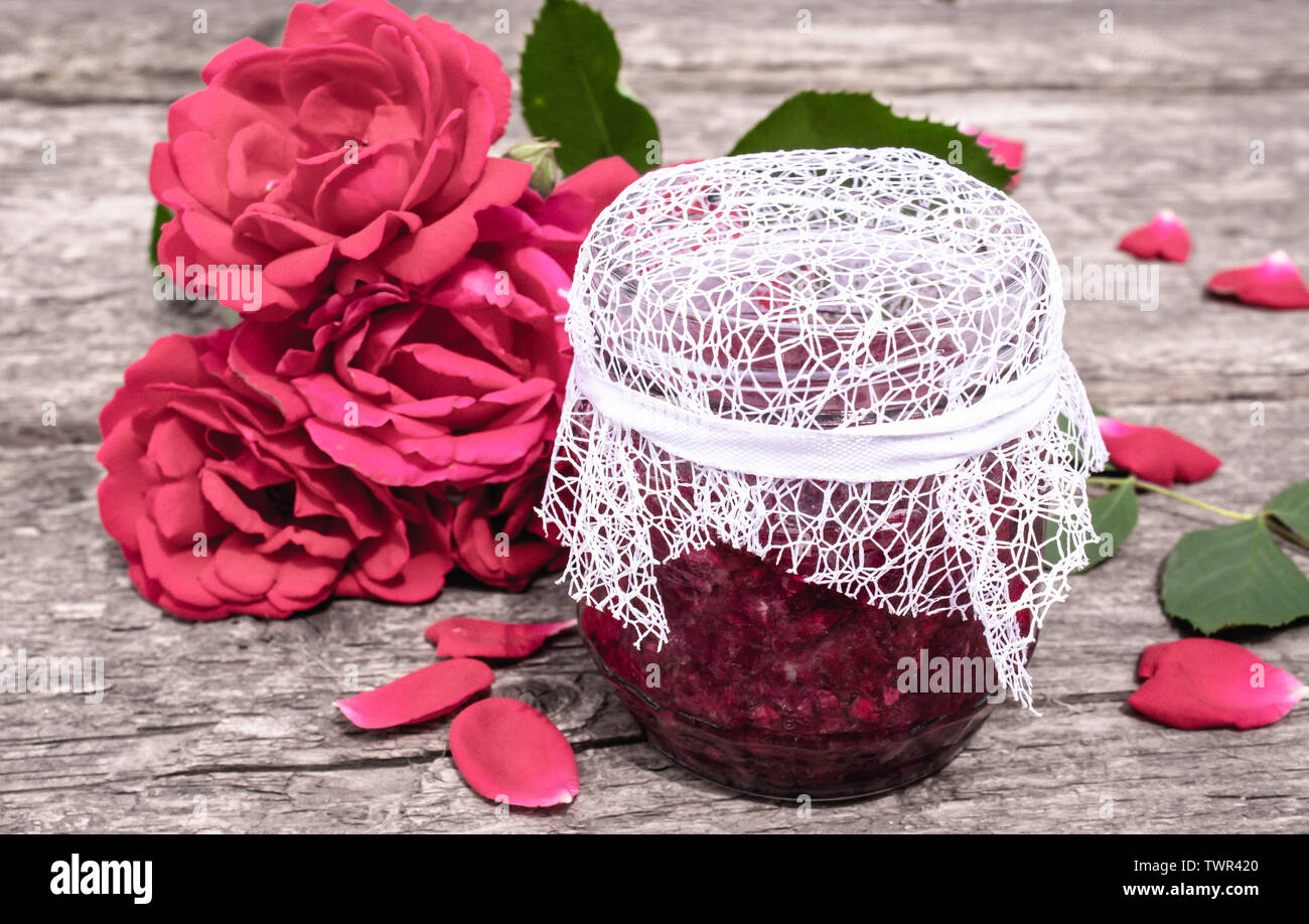 Jar of jam of rose petals on a wooden table with flowers of roses ...