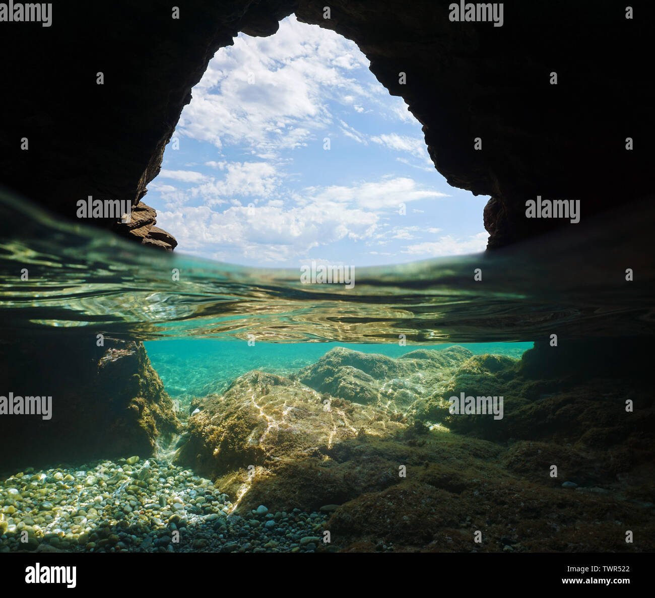 Inside a cave on the sea shore, blue sky with clouds and rocks ...