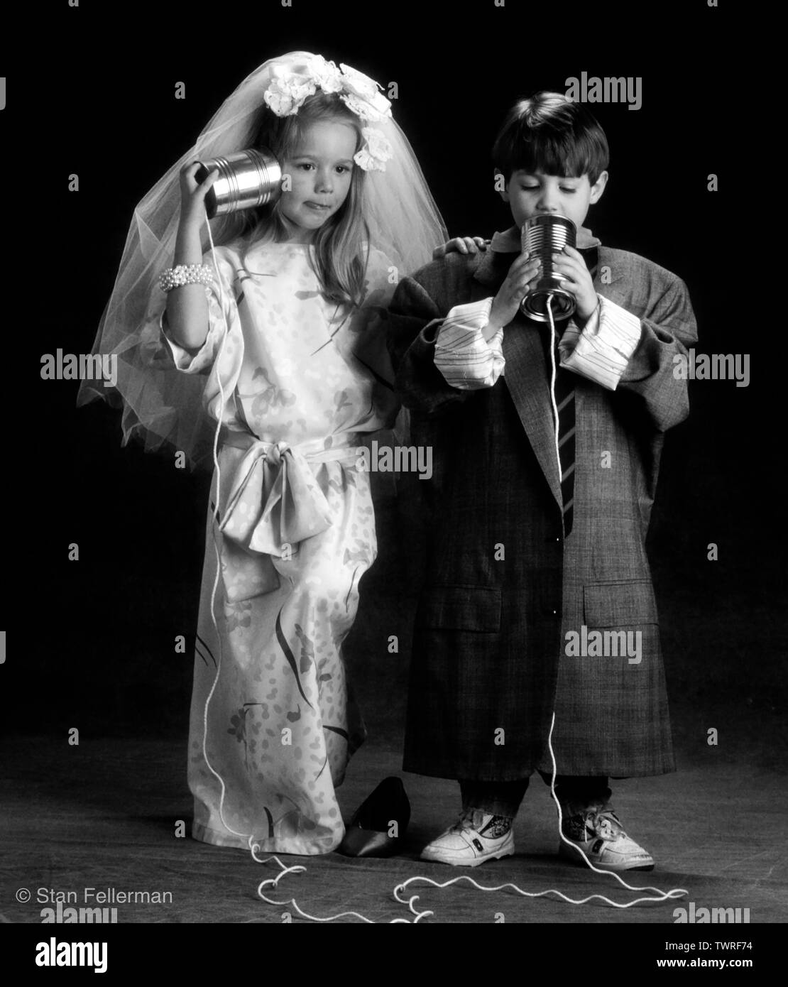 Two children getting married wearing adult clothes talking on can on a ...