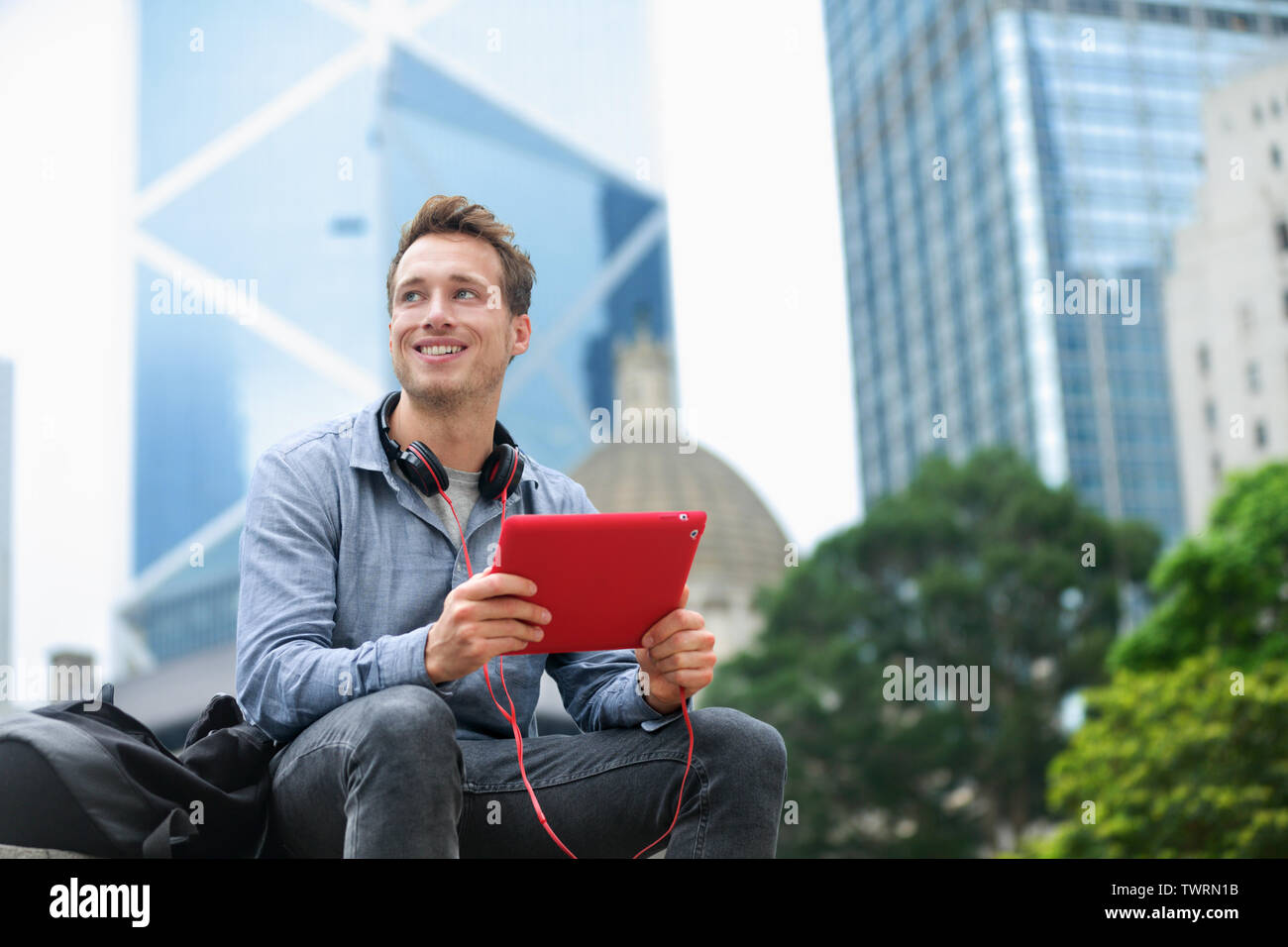 Urban man using tablet computer sitting in Hong Kong outside using app ...