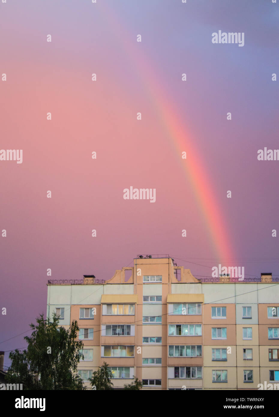 Rainbow over the roof of a multi-storey city house in the evening pink ...