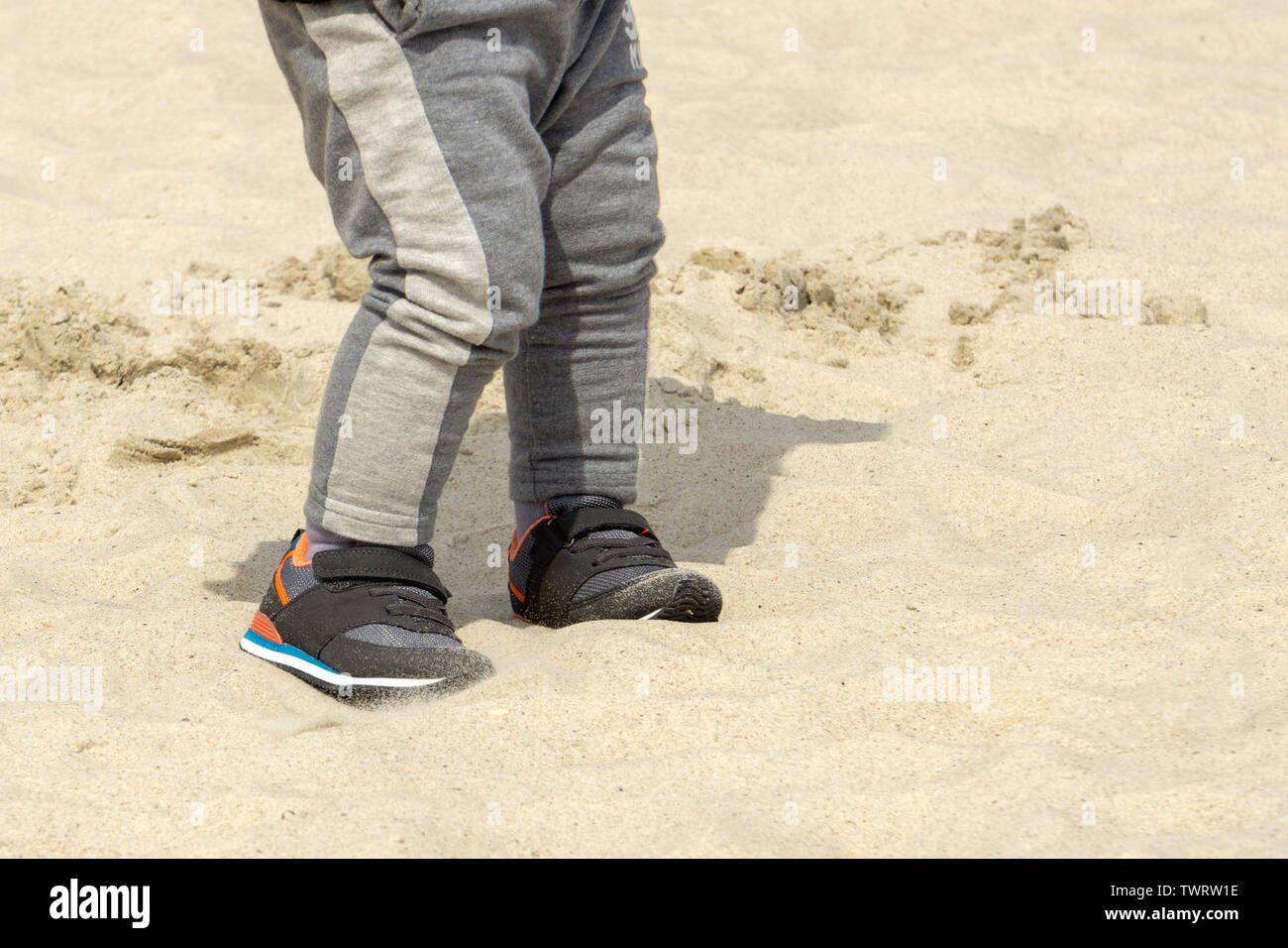 The feet of the baby in gray pants and sneakers stand uncertainly on ...