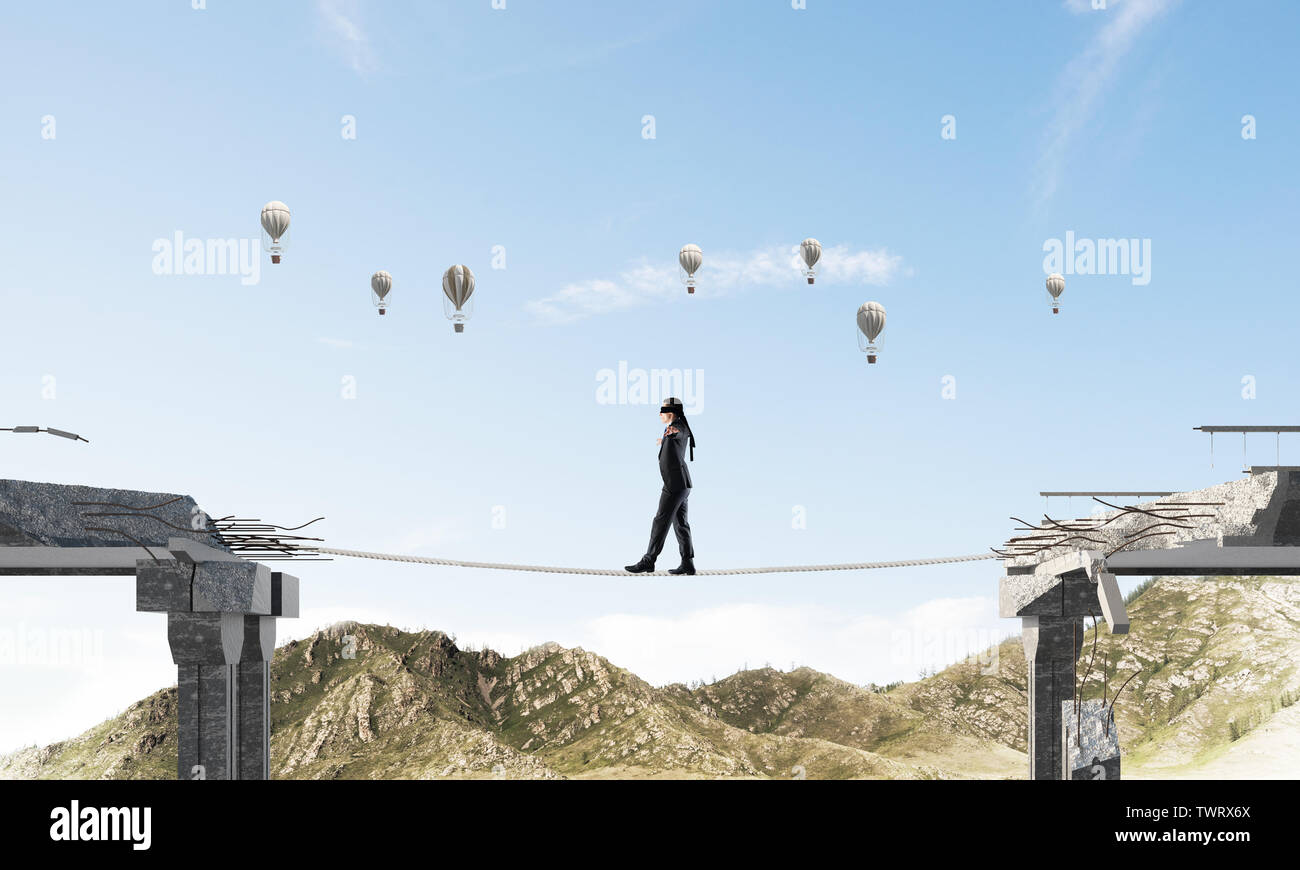 Businessman walking blindfolded on rope above huge gap in bridge as ...