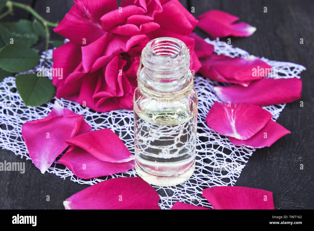 Essential oil with red rose petals on a dark wooden background ...