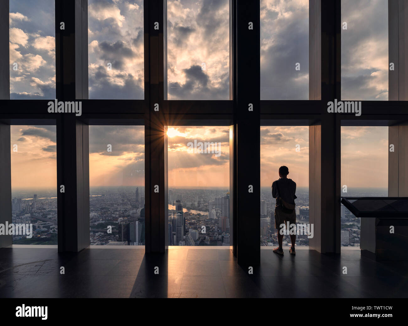 Man standing and sightseeing the bangkok city through windows at sunset ...