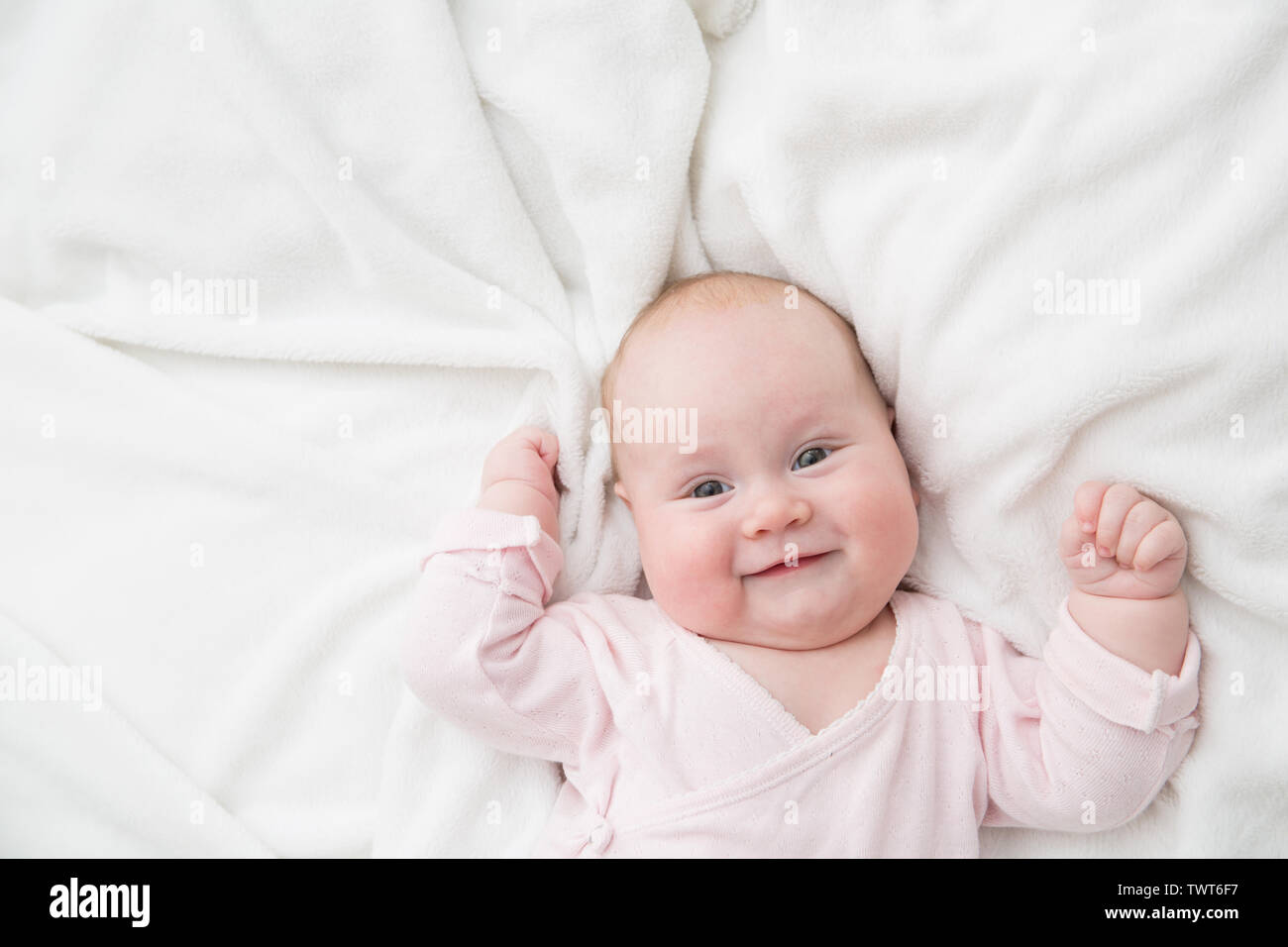 Newborn baby girl posed on her back, on blanket of fur, smiling looking ...