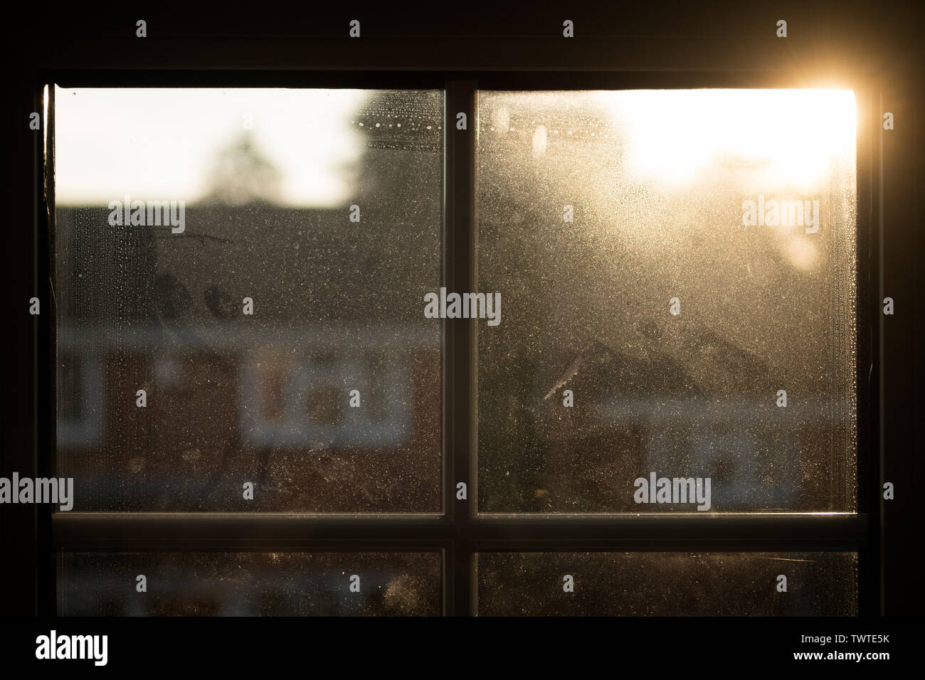 Sun rising over rooftop, seen through house window misted by dust and ...